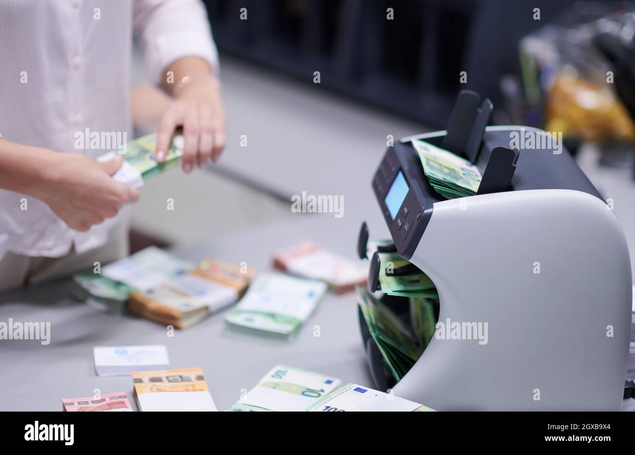 Bank employees using money counting machine while sorting and counting paper banknotes inside ...