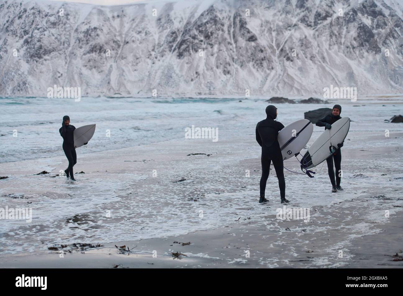 Authentic local Arctic surfers going by beach after surfing in Norwegian sea at snow capped ...