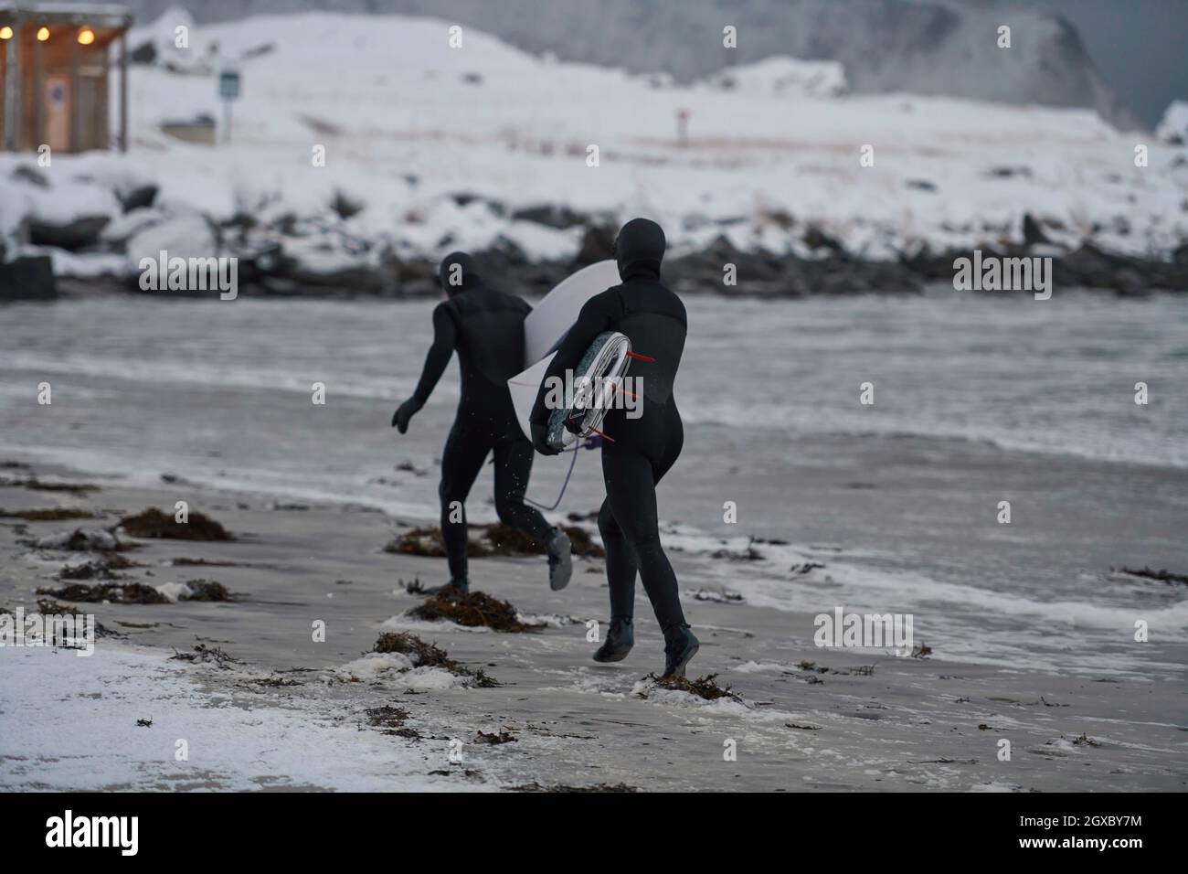Authentic local Arctic surfers running on snowy beach after surfing in ...