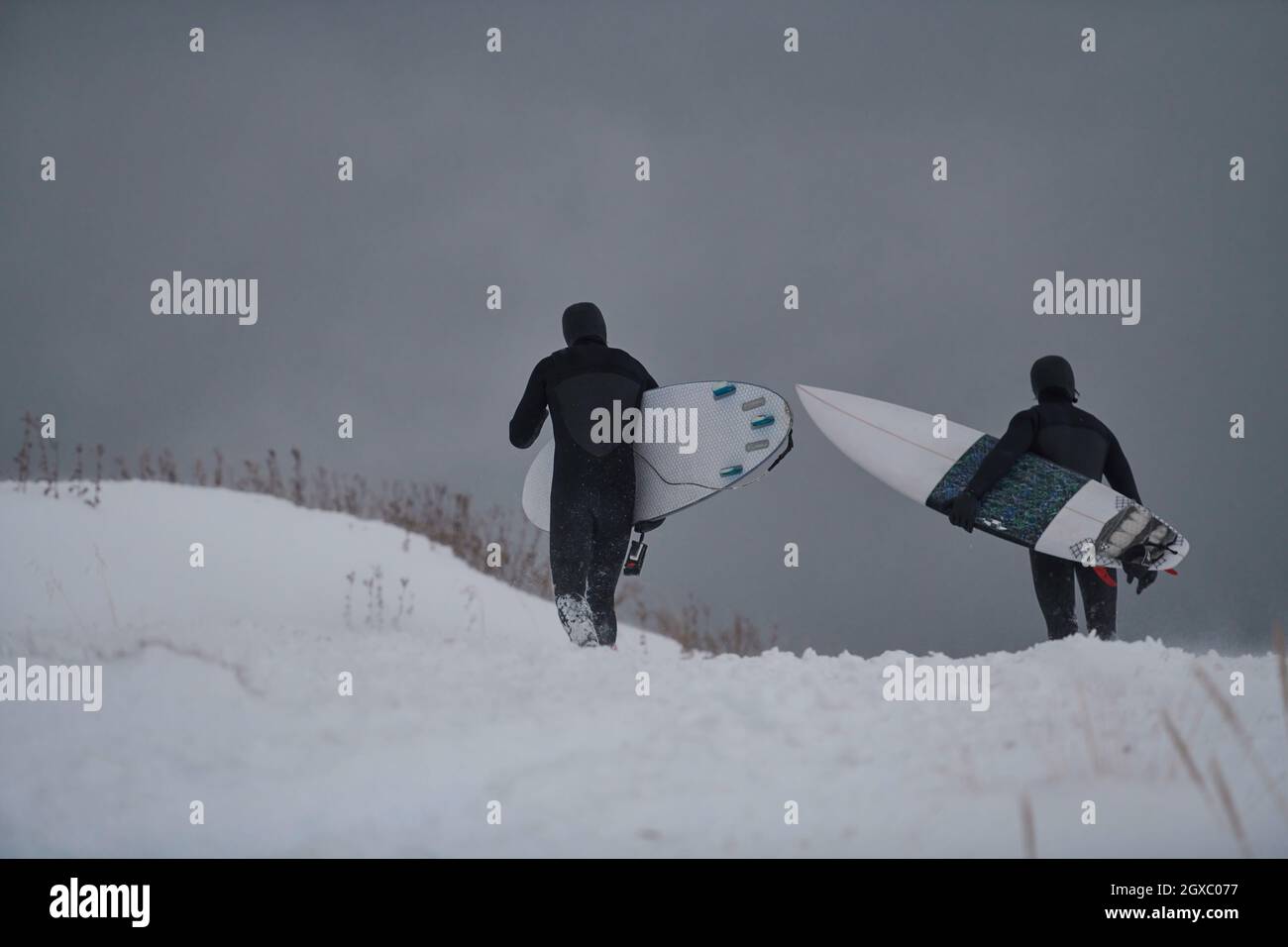 Authentic local Arctic surfers running on snowy beach after surfing in ...