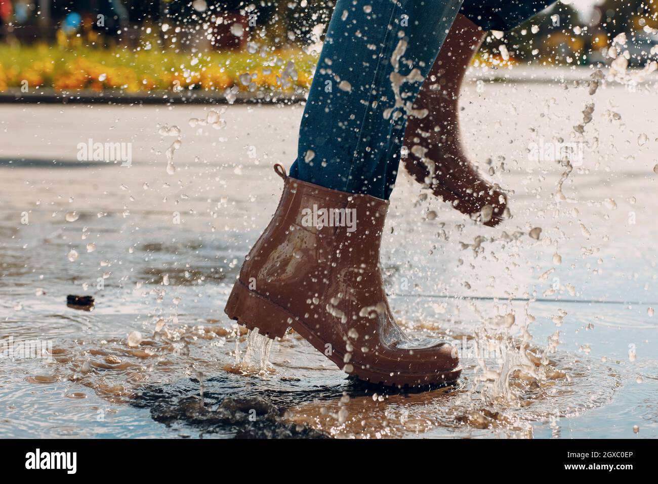 Woman wearing rain rubber boots walking running and jumping into puddle with water splash and ...