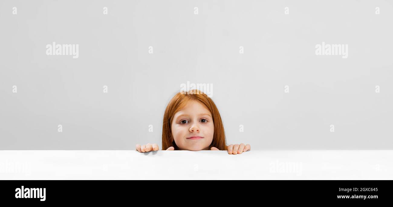 Portrait of little girl, child in casual peeking out table isolated ...