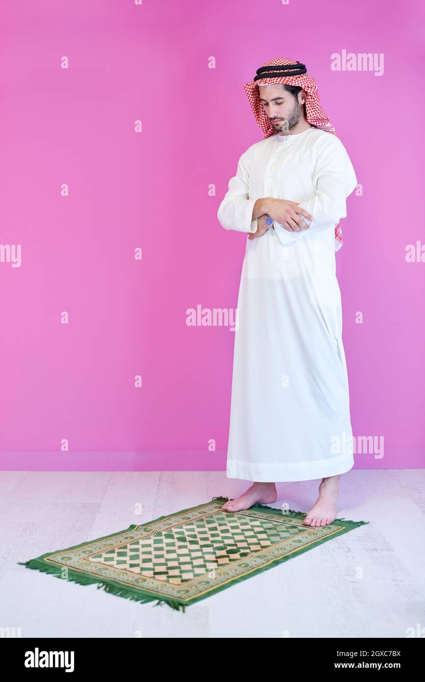 young arabian muslim man in traditional clothes praying on the carpet ...