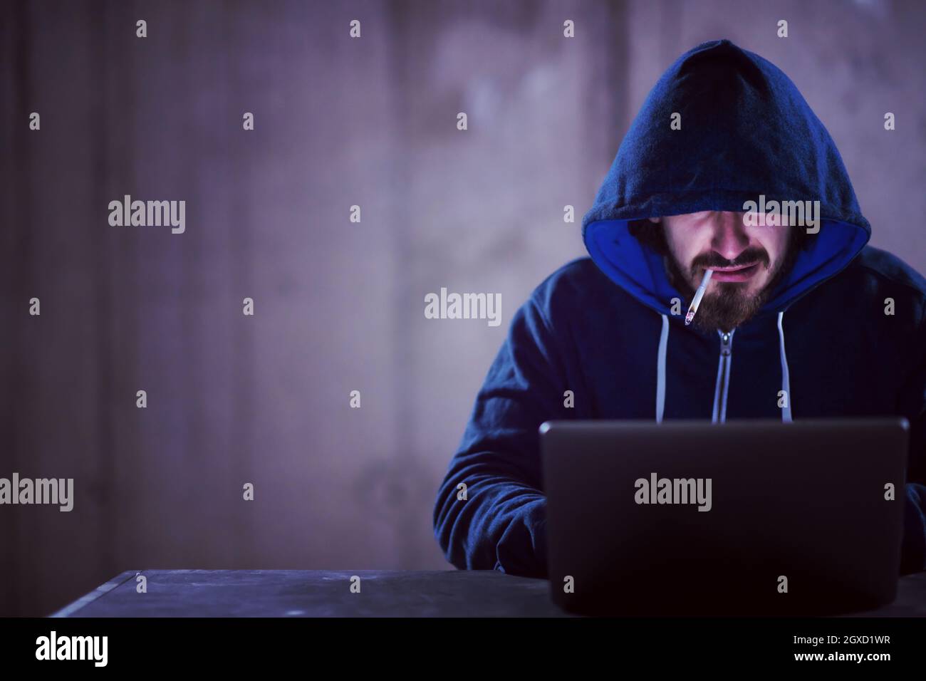 Young talented hacker smoking cigarette while working on laptop ...