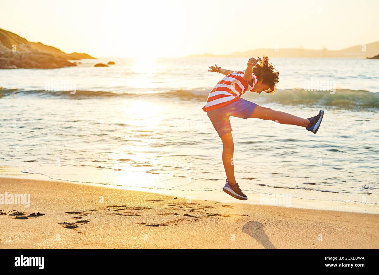 Back view full length of boy outstretching hands while leaping up on ...