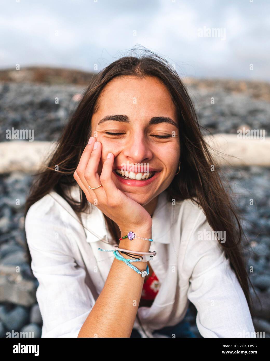 Mindful female teenager with toothy smile and closed eyes touching face ...