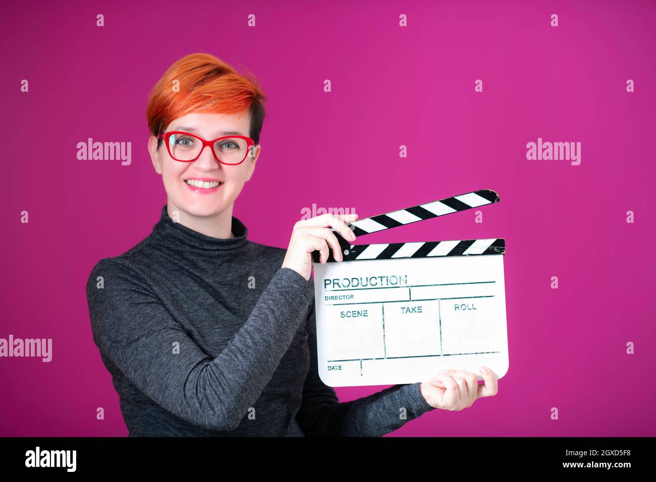 redhead woman holding movie clapper isolated against pink background ...