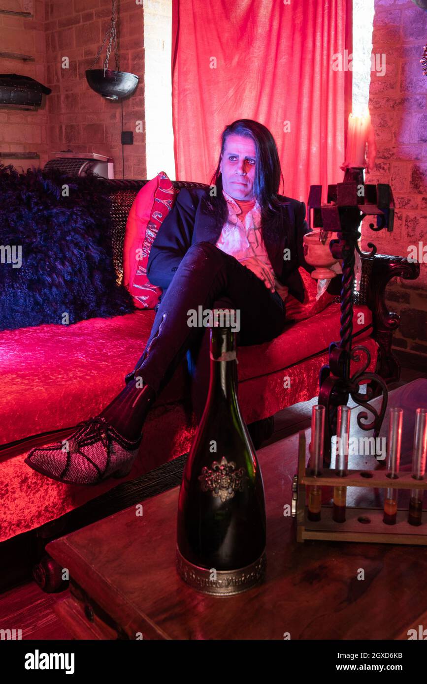 A disturbing man sitting on a red sofa in a Gothic-medieval setting ...