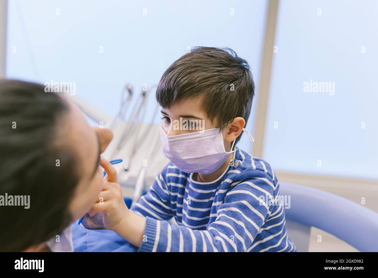 Curious boy in medical mask playing role of dentist and checking teeth ...