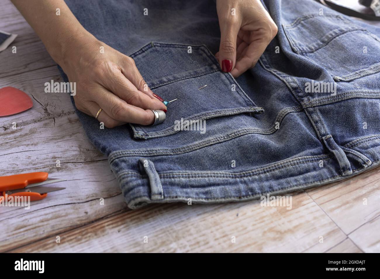 From above of crop Woman sewer attaching pin to jeans on wooden table ...