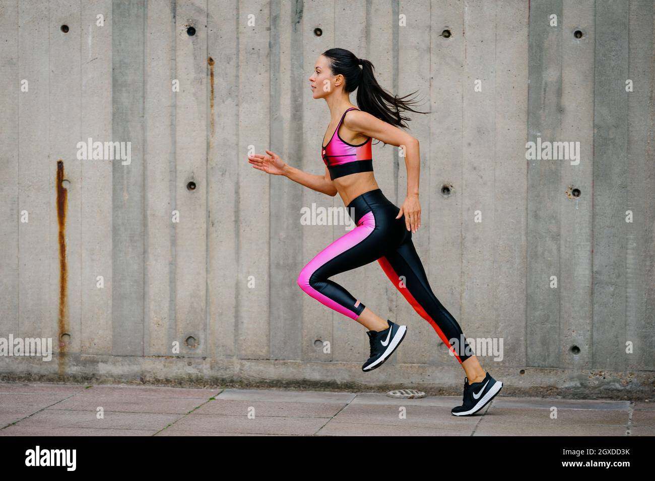 An athletic woman in a pink sports outfit running in an urban ...
