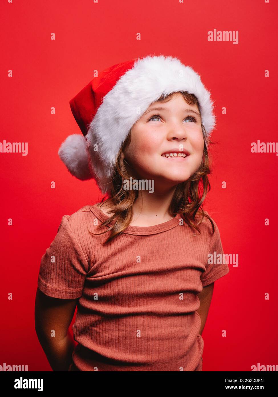 Adorable happy little girl in casual clothes and Santa hat smiling ...