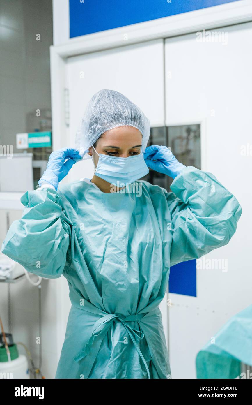 Young female veterinary surgeon in green uniform putting on disposable ...