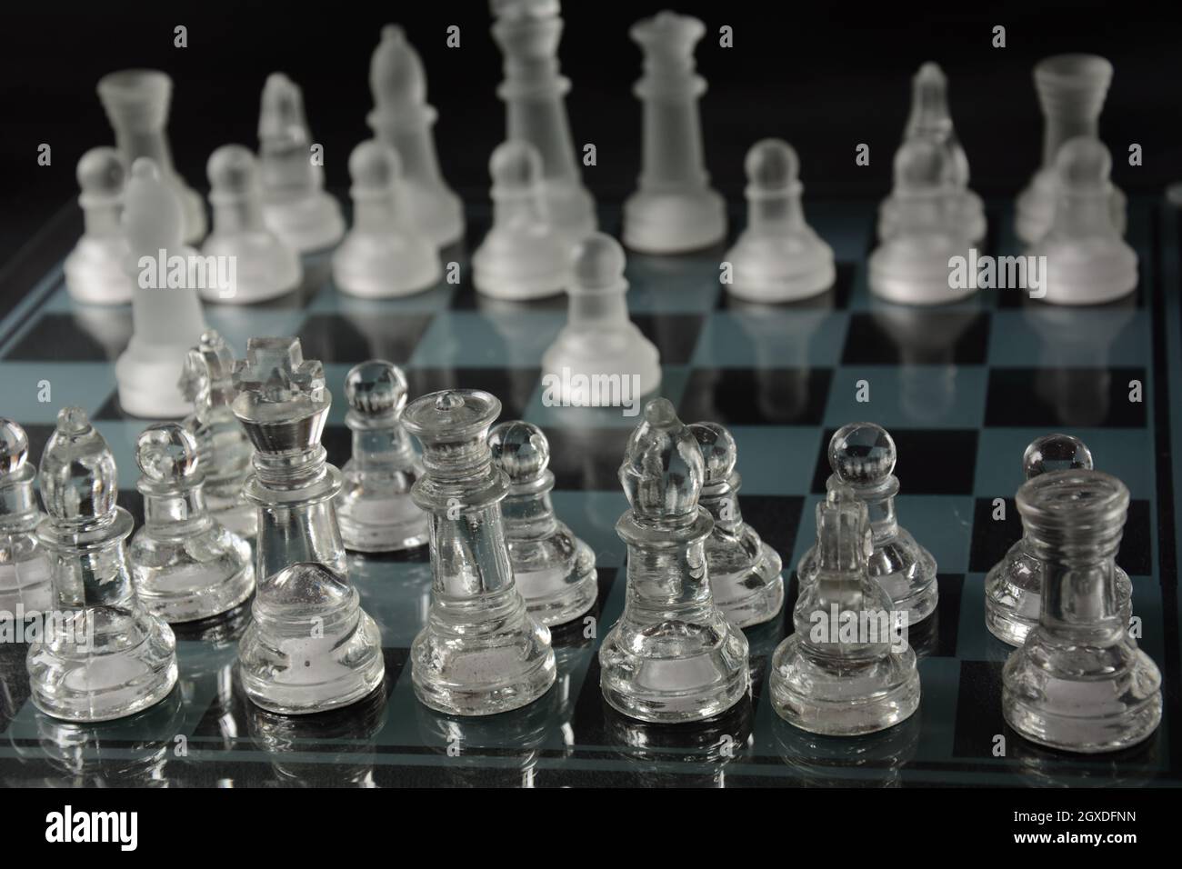 Clear glass chess pieces on a glass chessboard isolated on a black ...