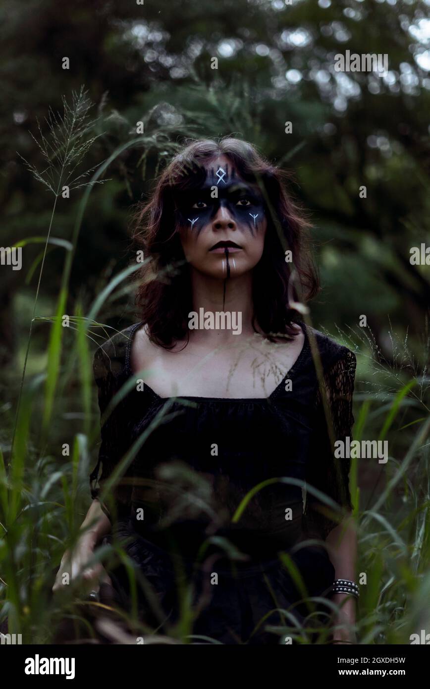 Mystic witch in long black dress and with painted face standing looking ...