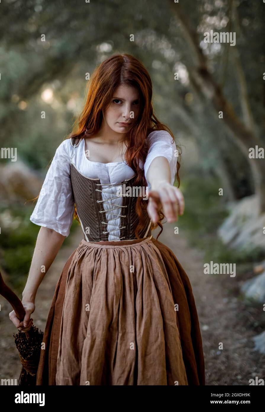 Mystic witch in dress and with broomstick pointing at camera while ...