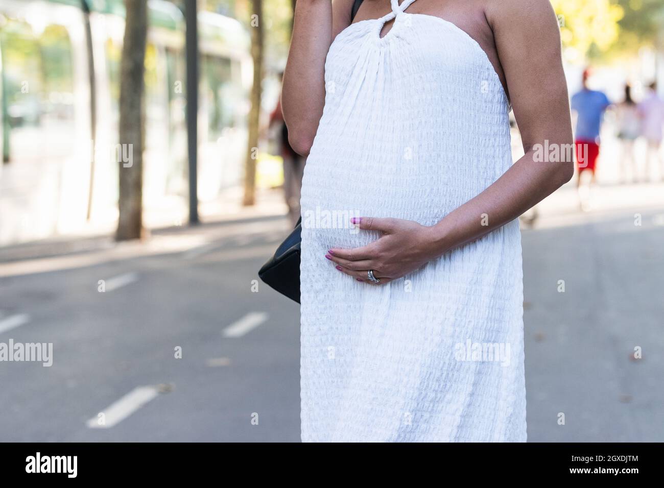 Cropped unrecognizable pregnant African American wearing white dress while walking on the street ...