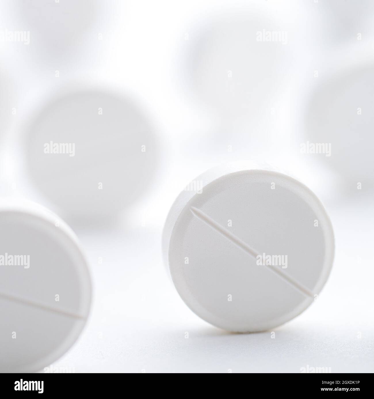 A pile of white pills scattered on a bright white background. Selective ...