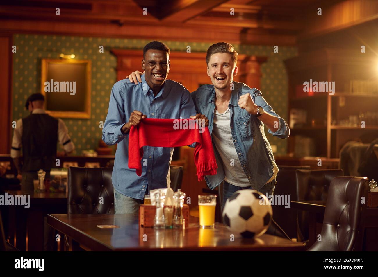 Two male football fans with red scarf and ball watching game tv ...