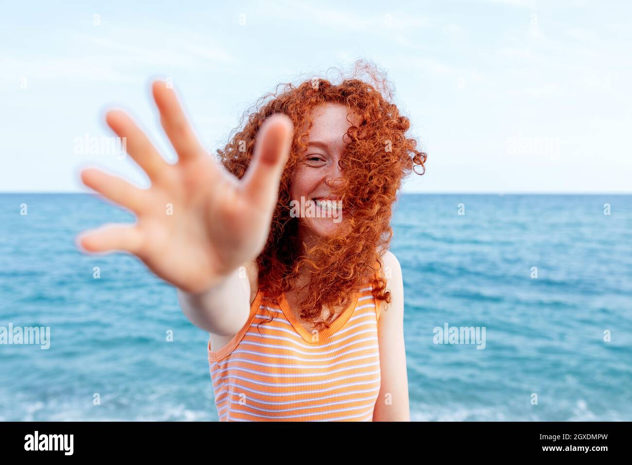 Optimistic young female with flying ginger hair reaching hand to camera ...