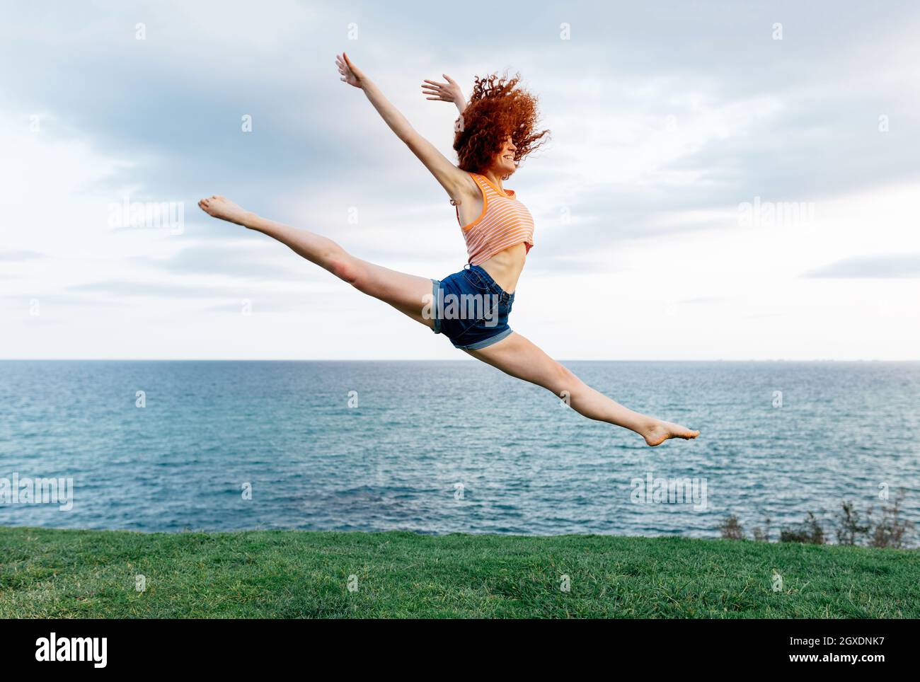 Full body of barefoot female doing split while jumping high with raised ...