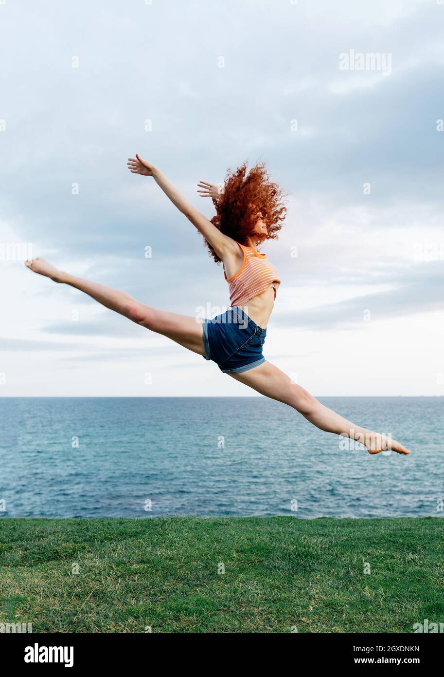 Full body of barefoot female doing split while jumping high with raised ...