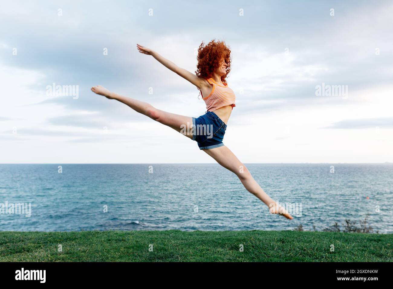 Full body of barefoot female doing split while jumping high with raised ...