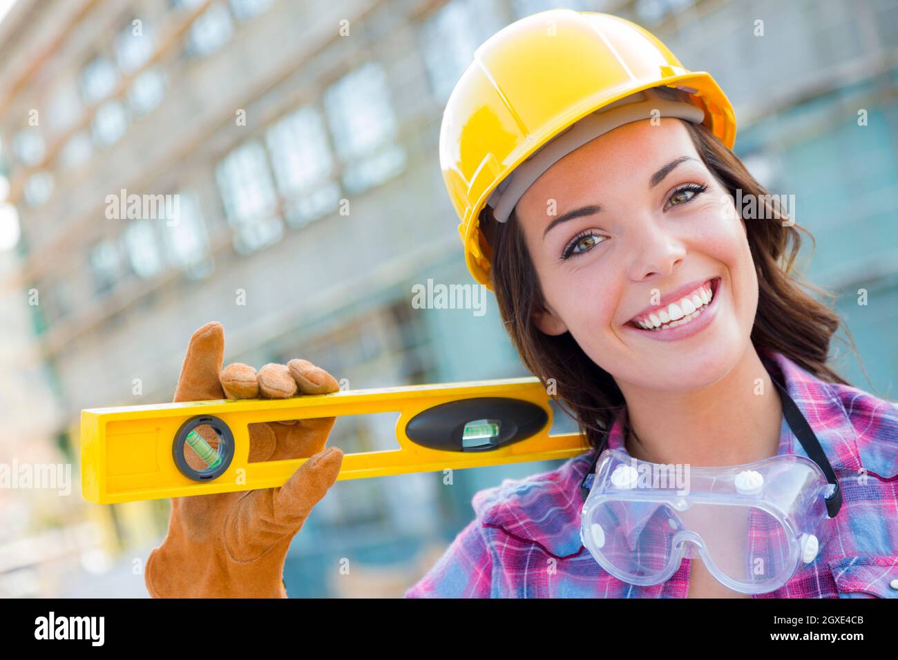 Portrait of Young Attractive Female Construction Worker with Level Wearing Gloves, Hard Hat and ...