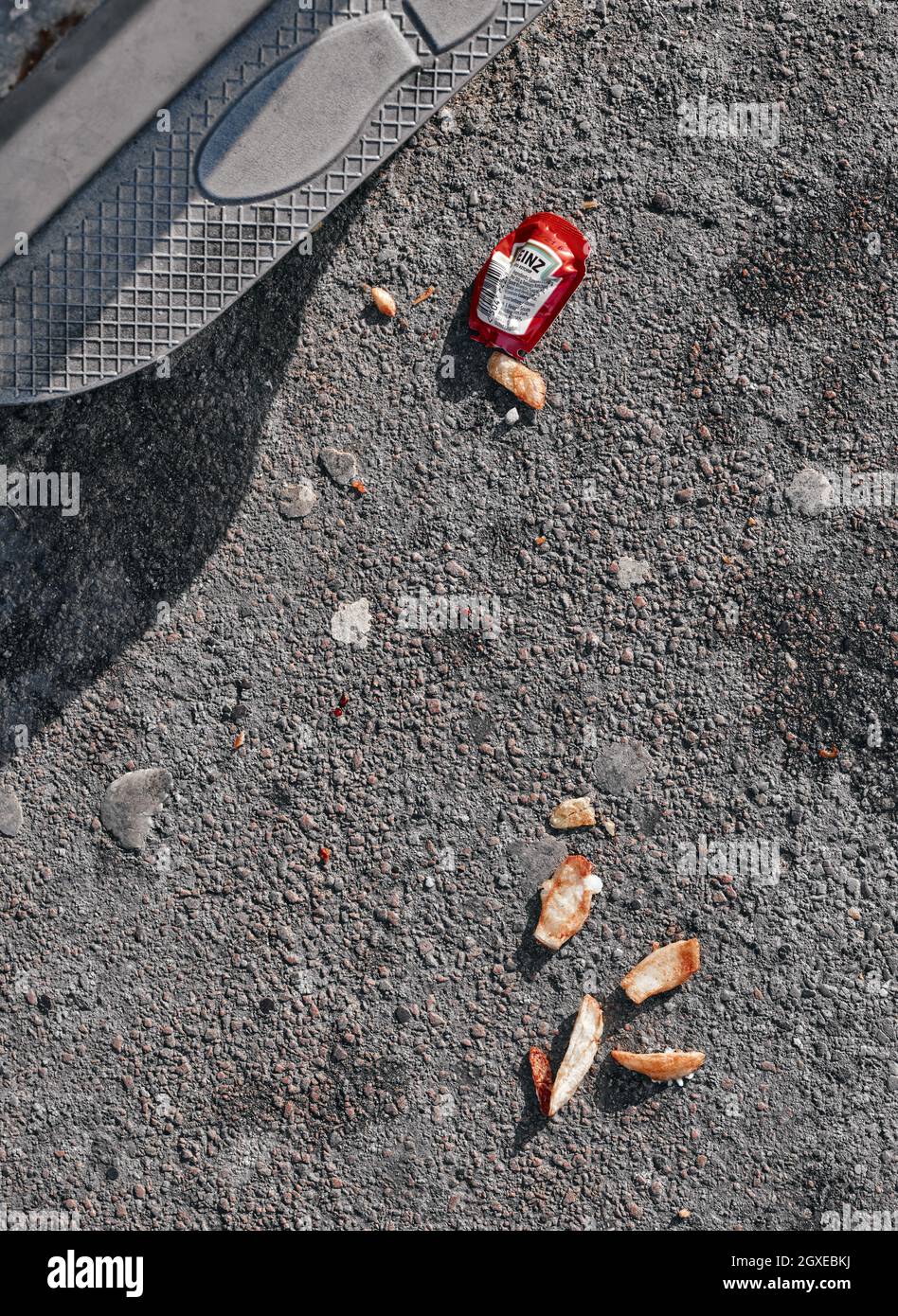 A used red Heinz Ketchup sachet / carton and chips discarded on the ...