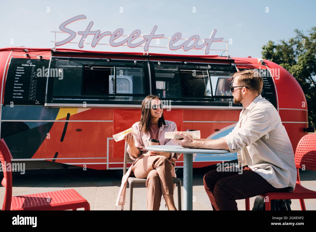 Young couple interacting while having fast food in outdoor cafe against ...