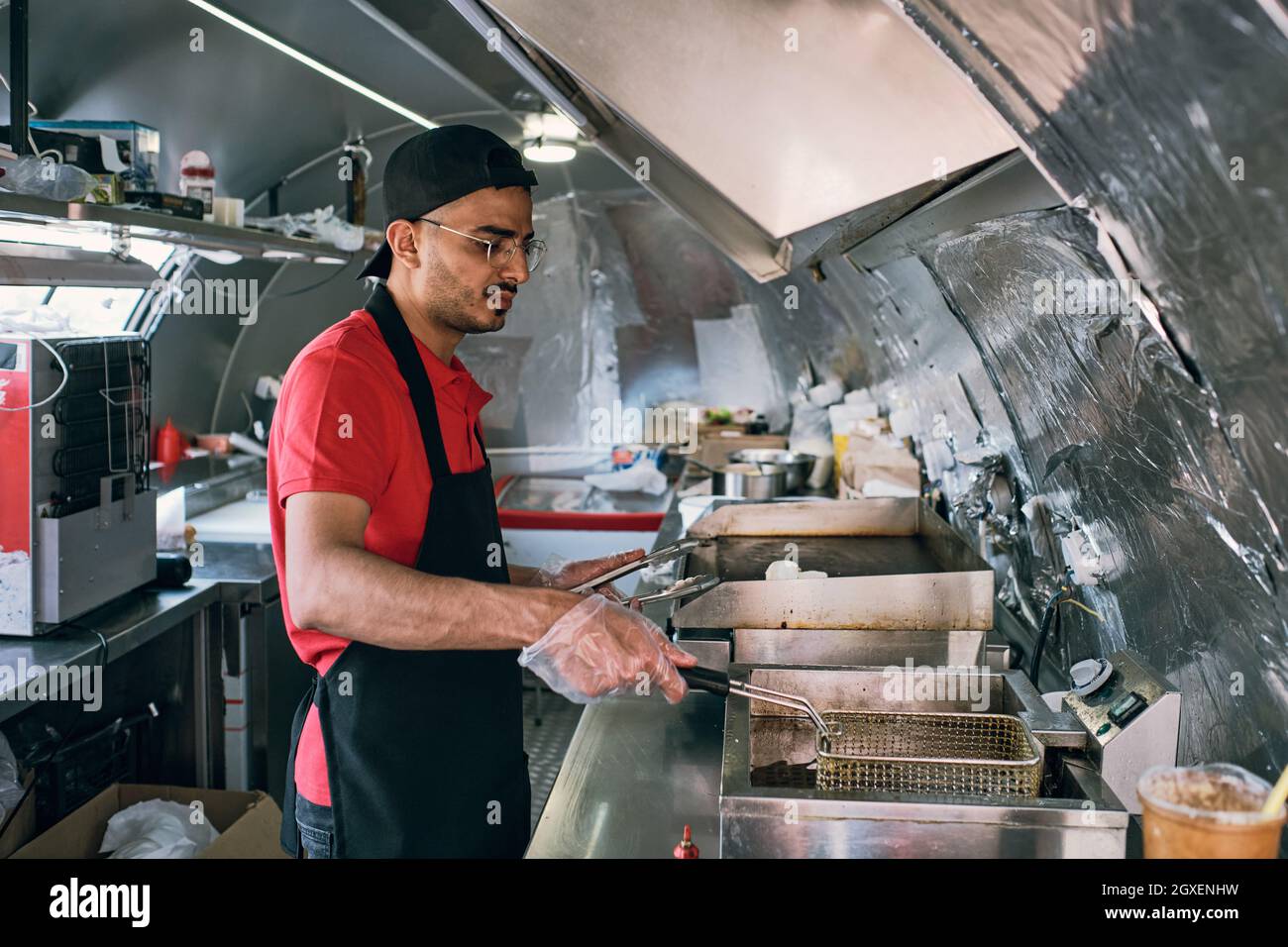 Young clerk of food truck frying snacks in large amount of oil or fat ... Young clerk of food truck frying snacks in large amount of oil or fat ...