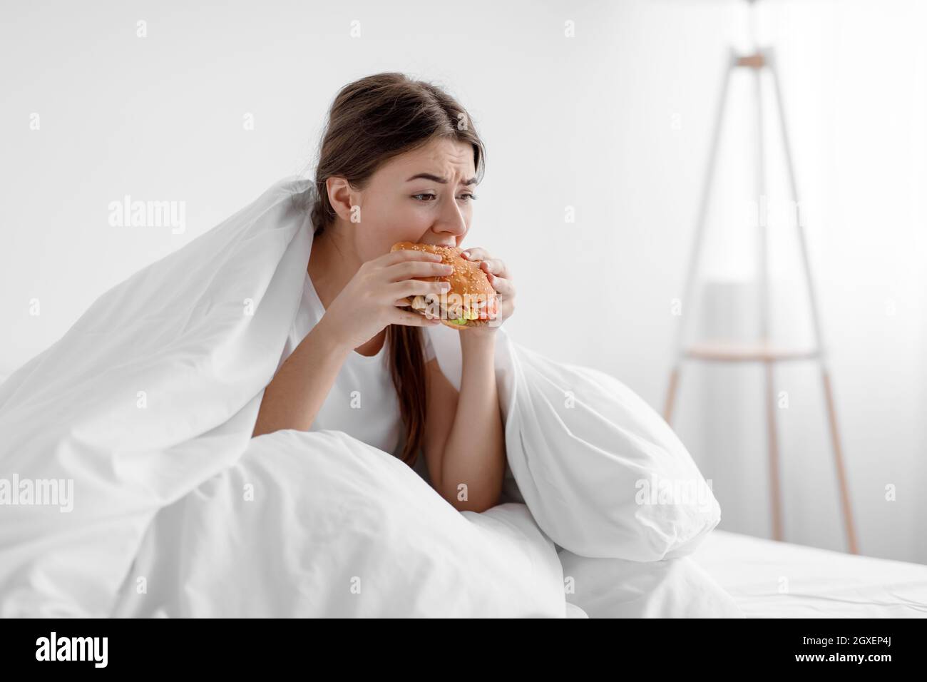 Starving upset hungry cute caucasian millennial woman sitting in bed at ...