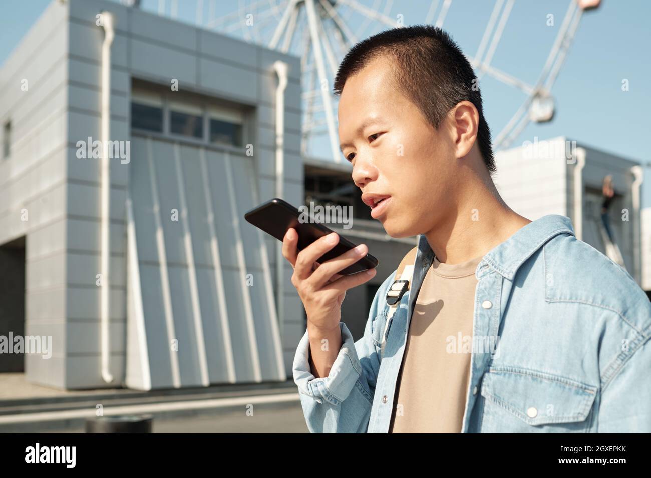Young man of Asian ethnicity recording voice message against modern ...