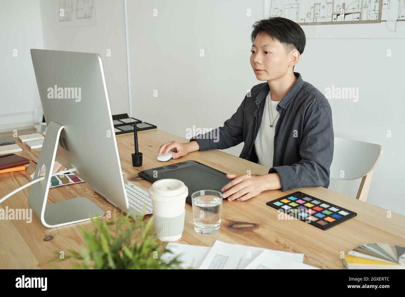 Young Chinese female designer sitting in front of computer monitor by ...