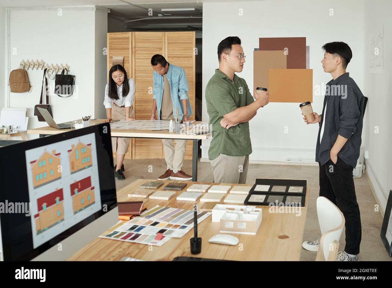 Two office workers with drinks discussing working points by workplace ...