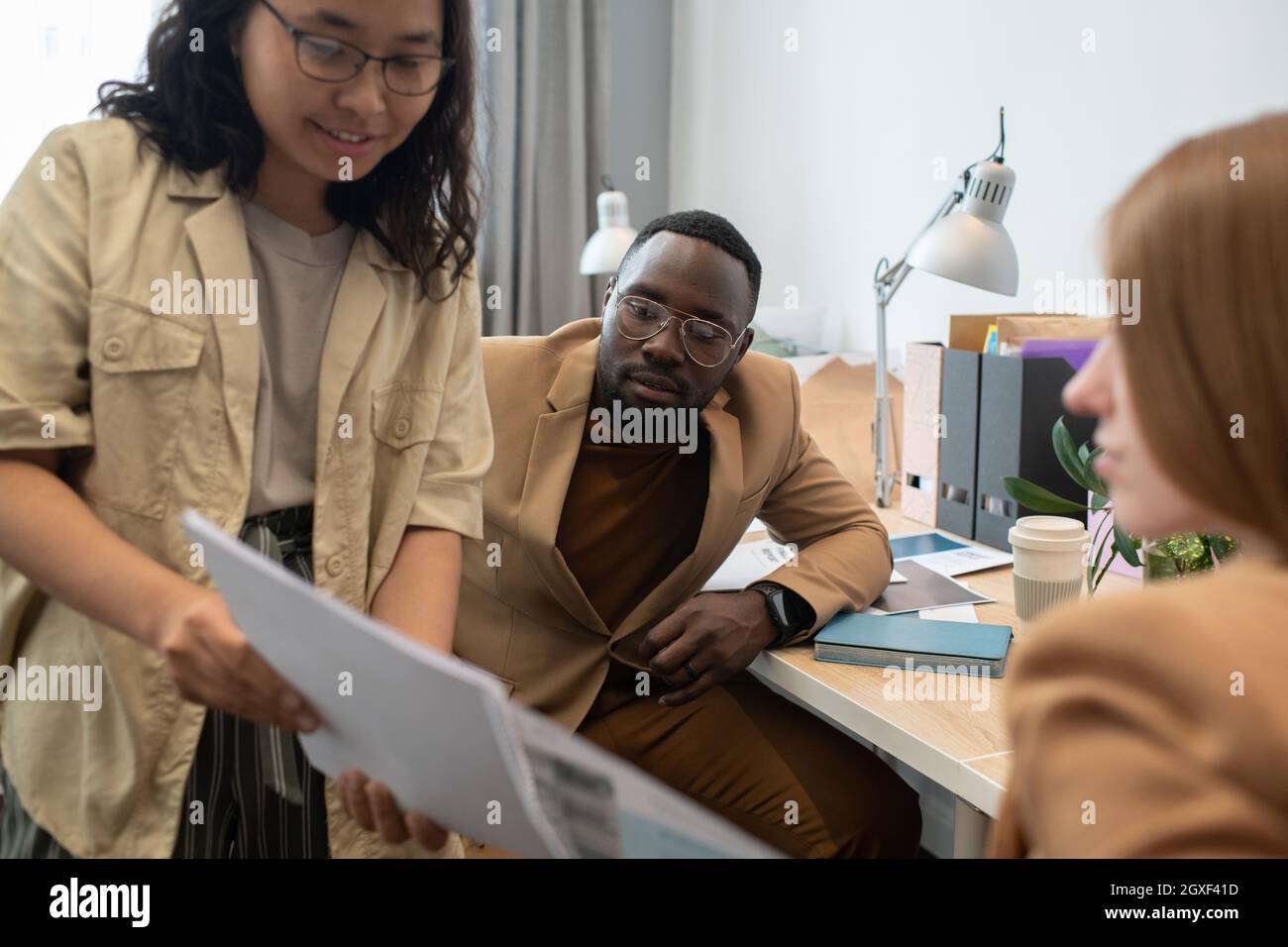 Serious businessman looking at paper held by young Asian colleague ...