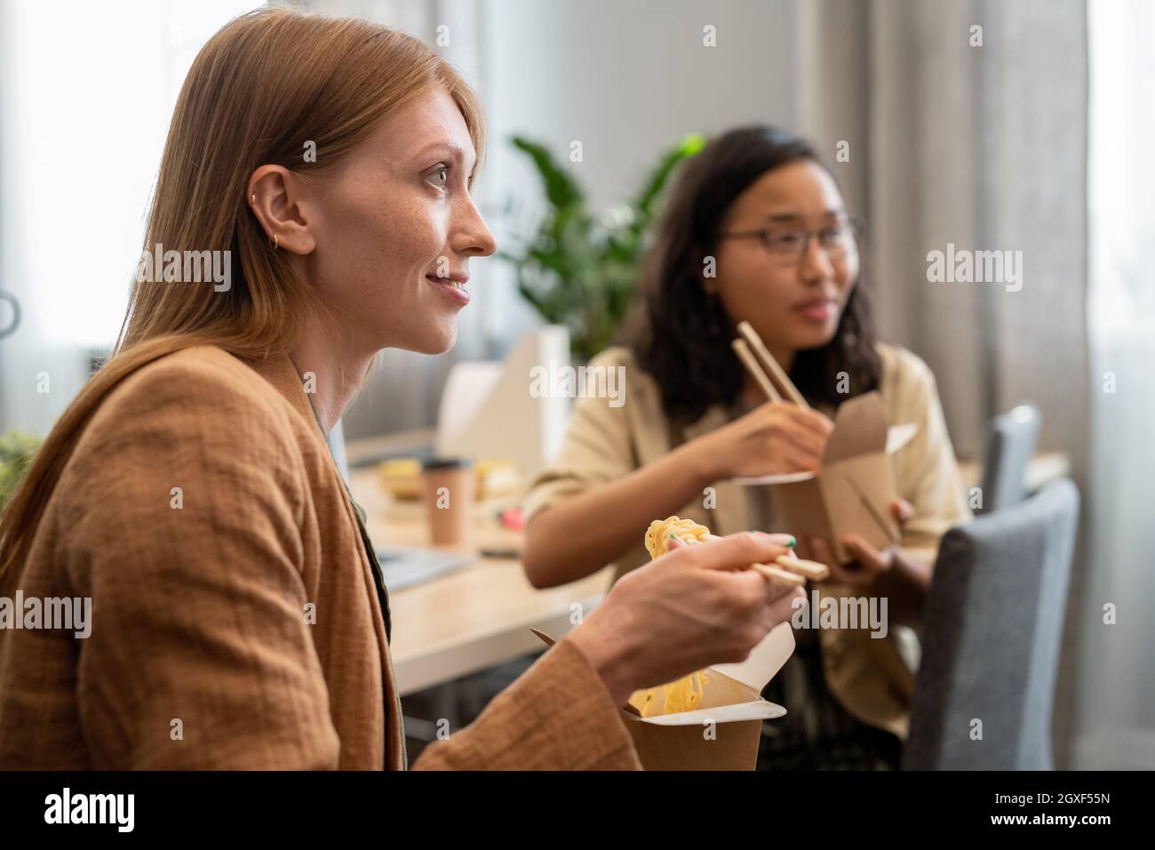 Happy young businesswoman and her colleague eating chinese wok at lunch ...