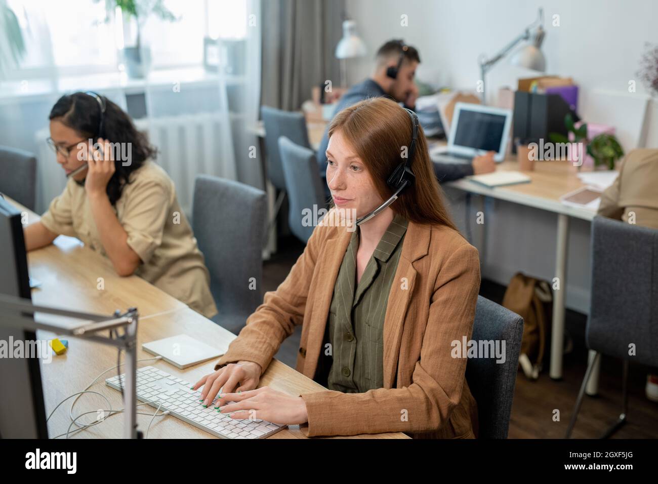 Young female operator of call center consulting clients in front of ...