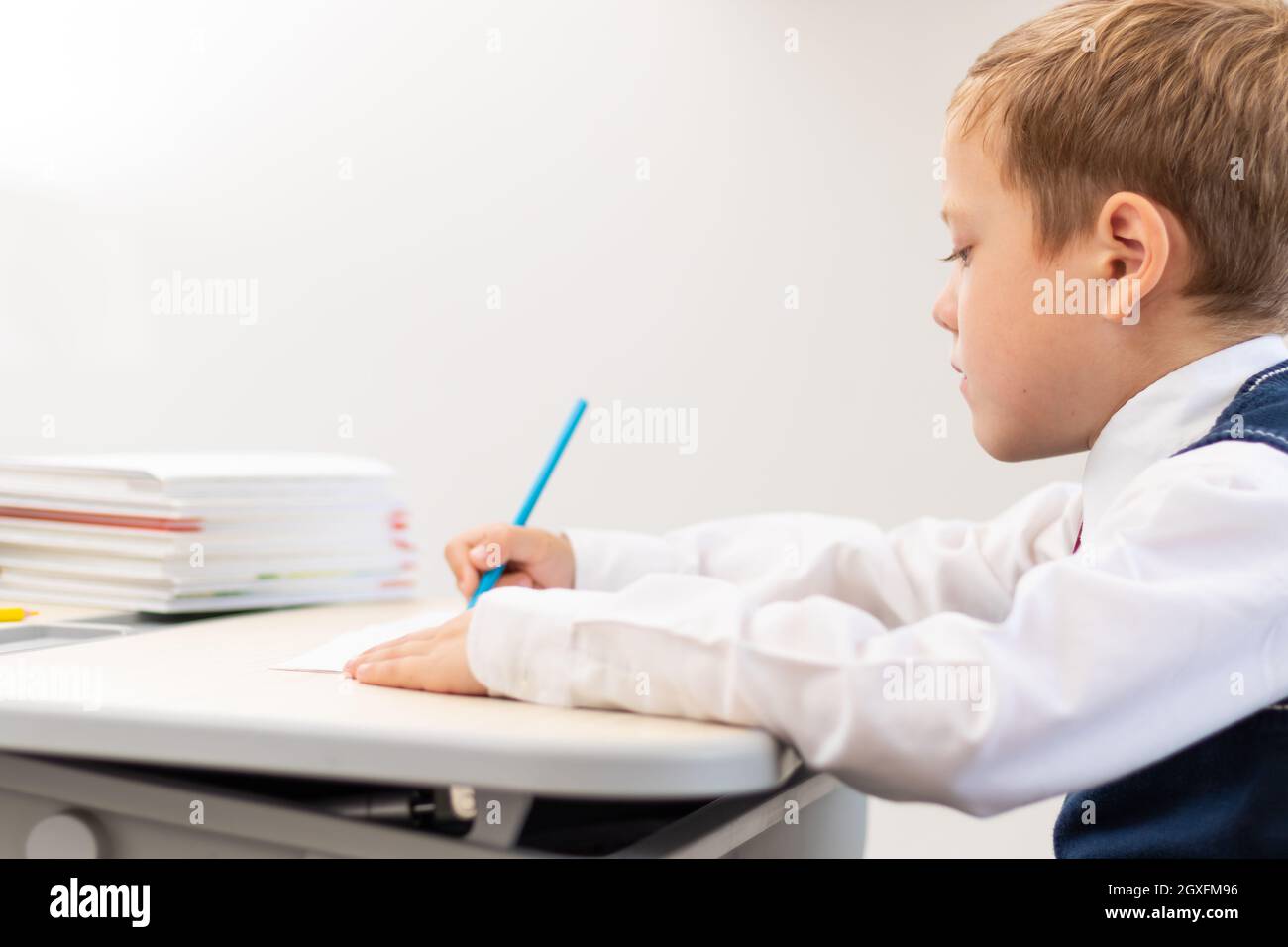 A cute boy first grader in a school uniform does homework while sitting ...