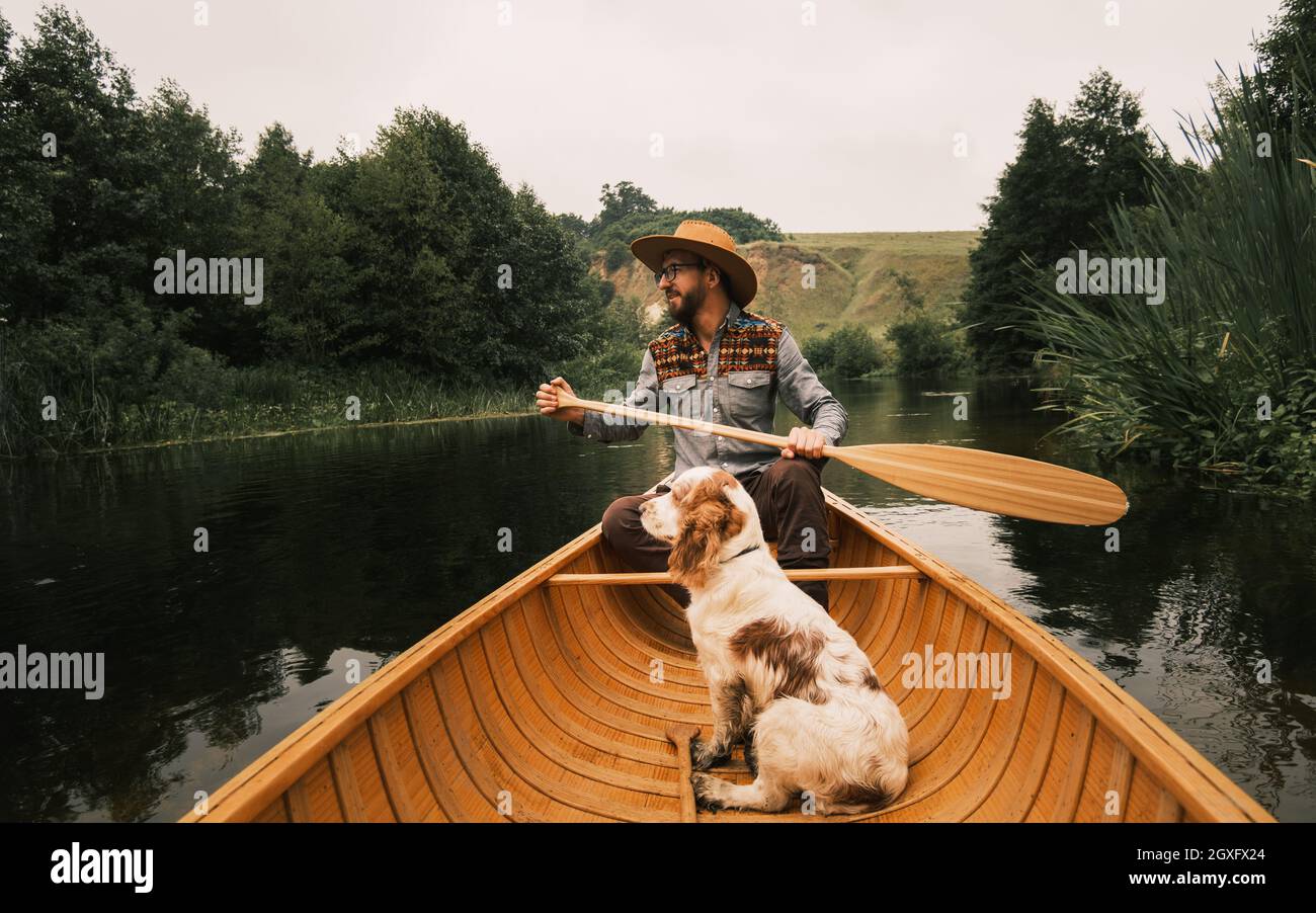 Wide angle shot: man and his dog in wooden canoe. Tranquil scene of ...