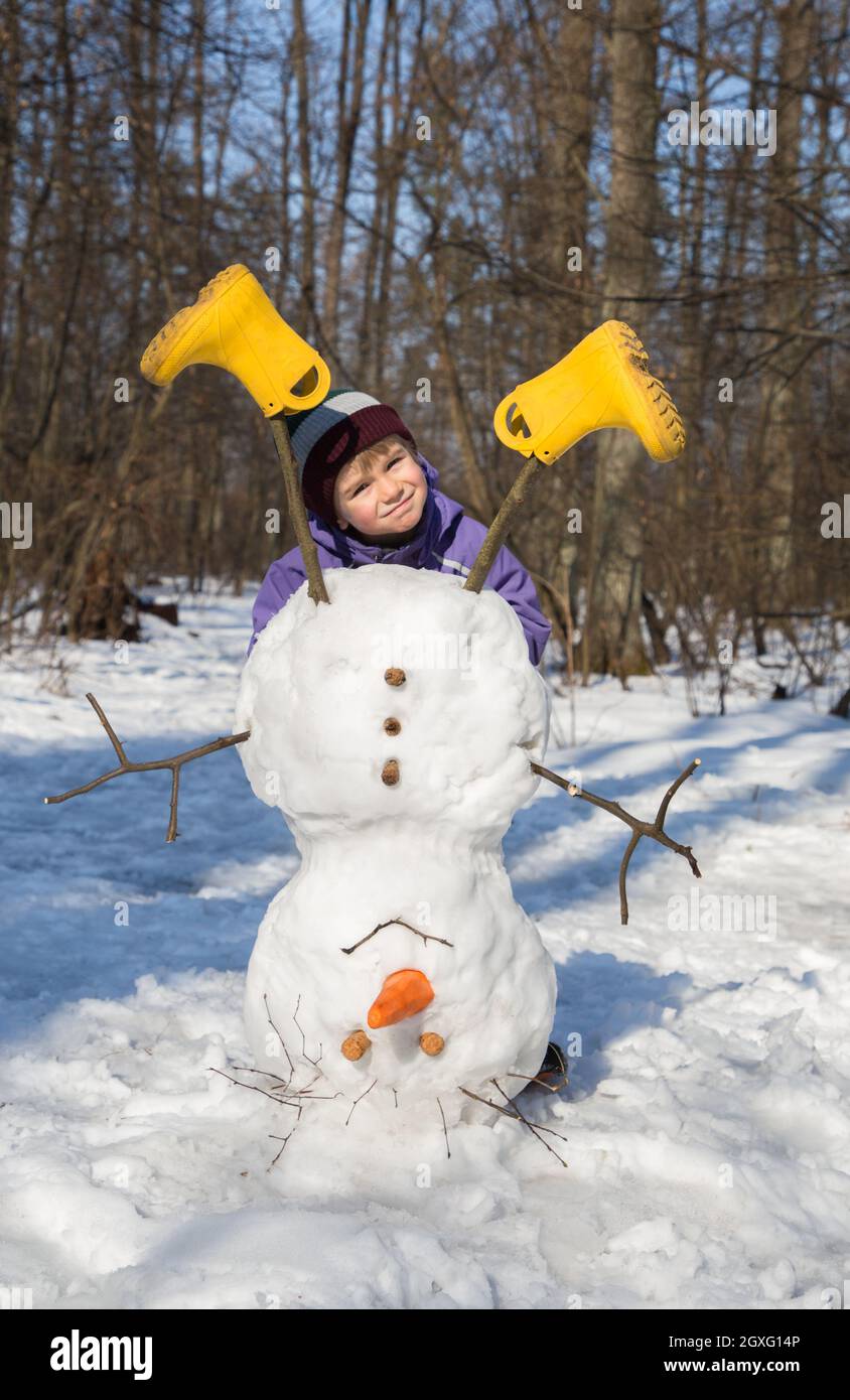 jolly cheerful snowman in yellow boots stands upside down in a snowy ...