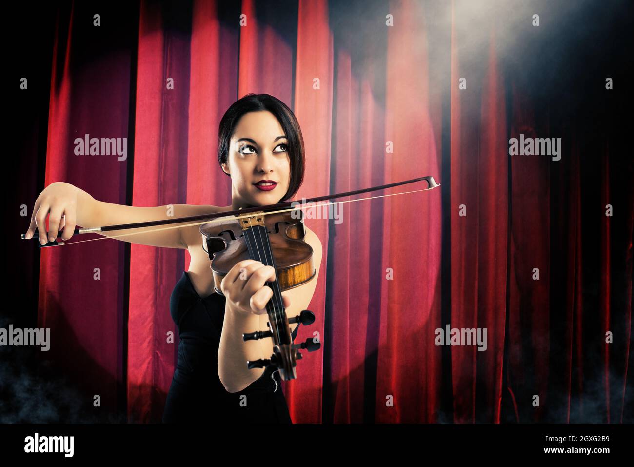 Elegant woman playing the violin with background of red curtains in a ...