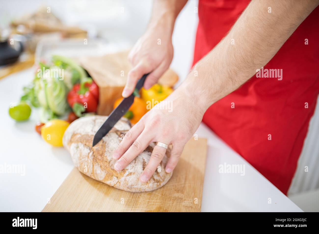 Male hands slicing bread on wooden cutting board above white table. Man ...