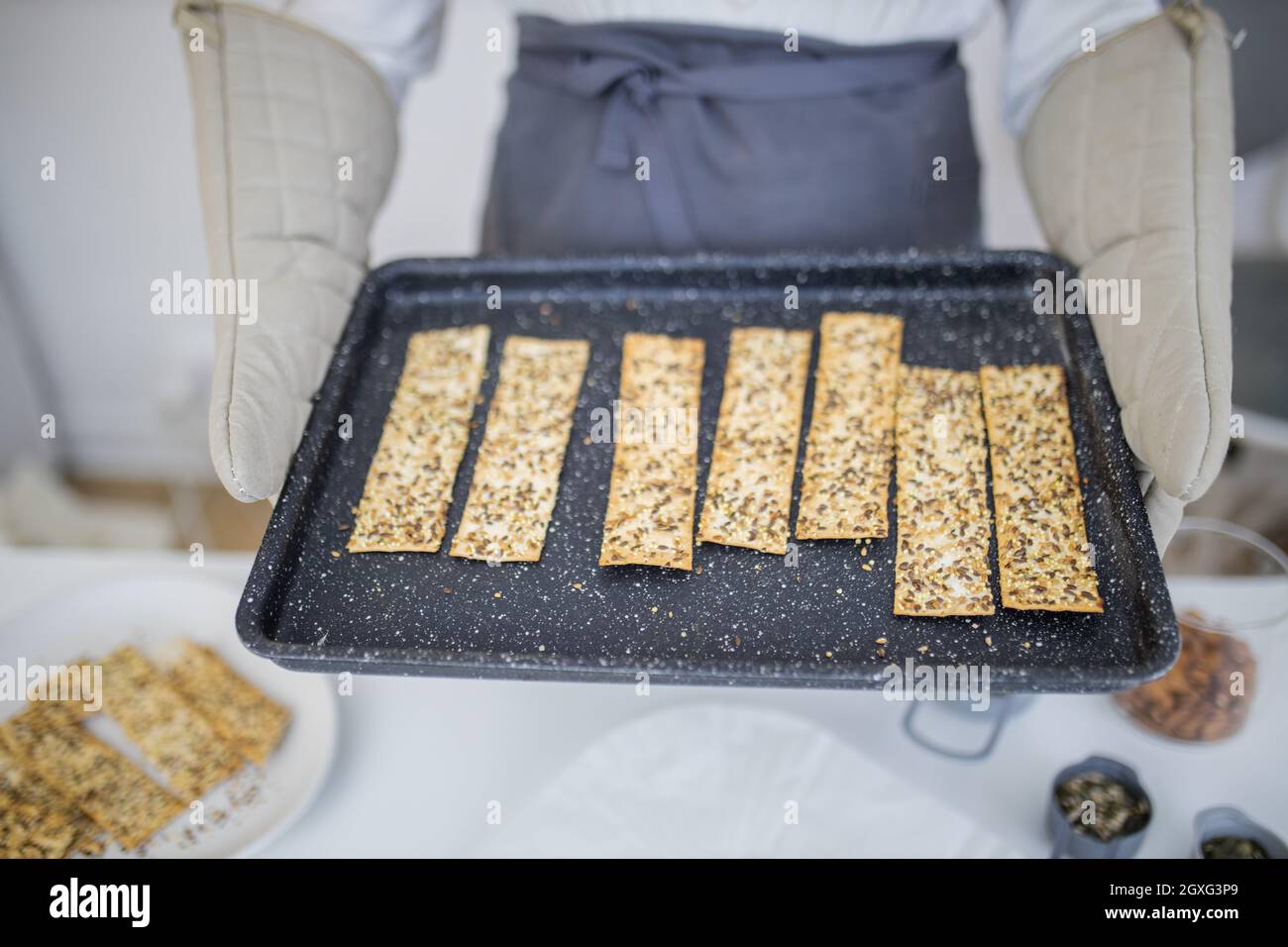 Gloved hands holding black tray of Swedish multi-seed crispbread ...
