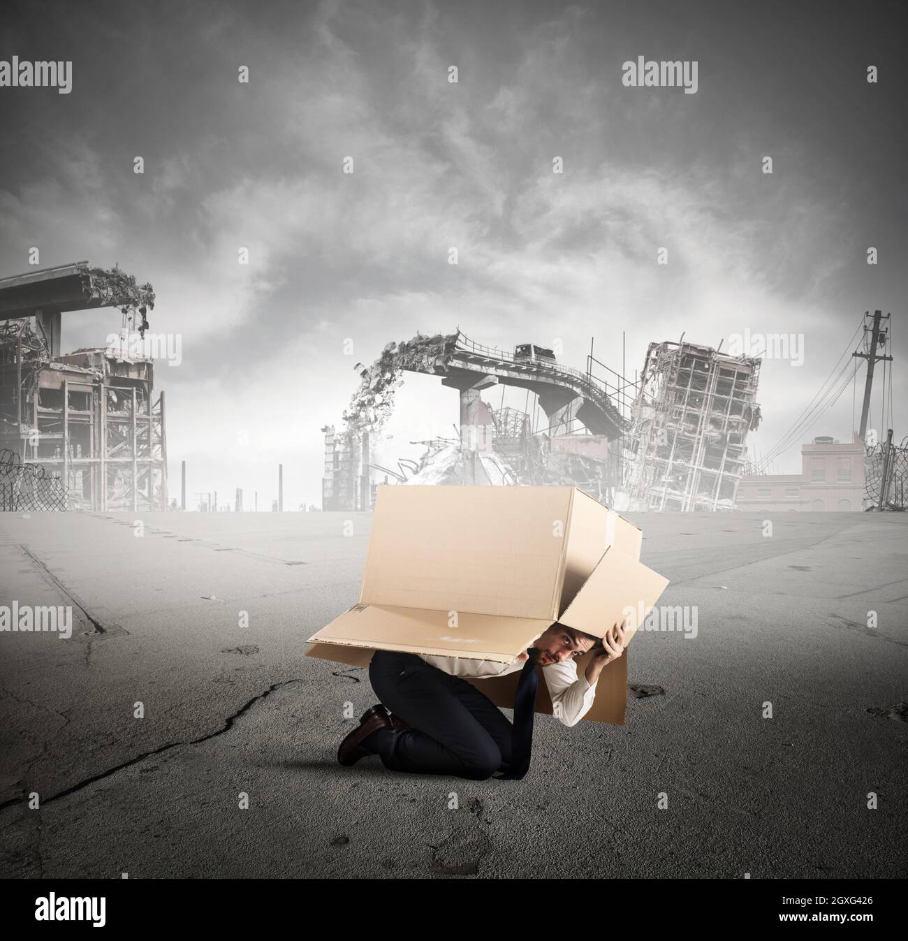 Afraid businessman is hiding under a cardboard in a city destroyed ...