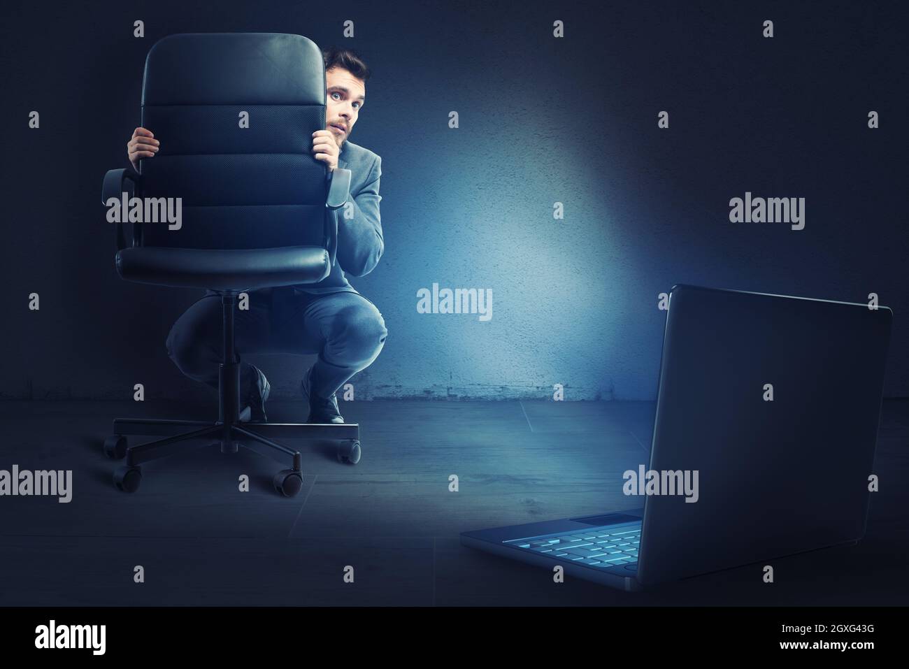 Afraid businessman hidden behind a chair looks his laptop Stock Photo ...