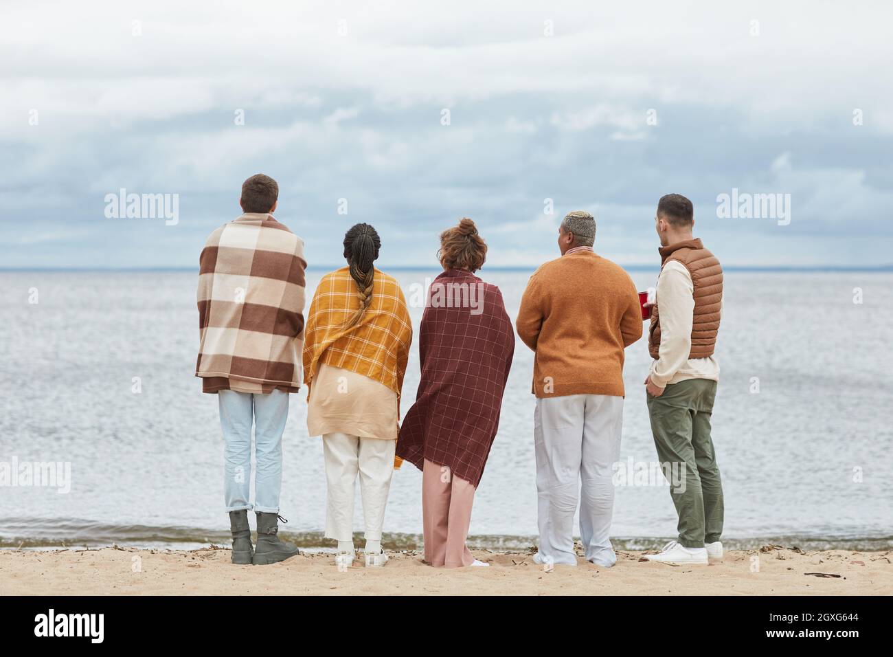 Back view at group of young people on beach in Autumn wrapped in ...
