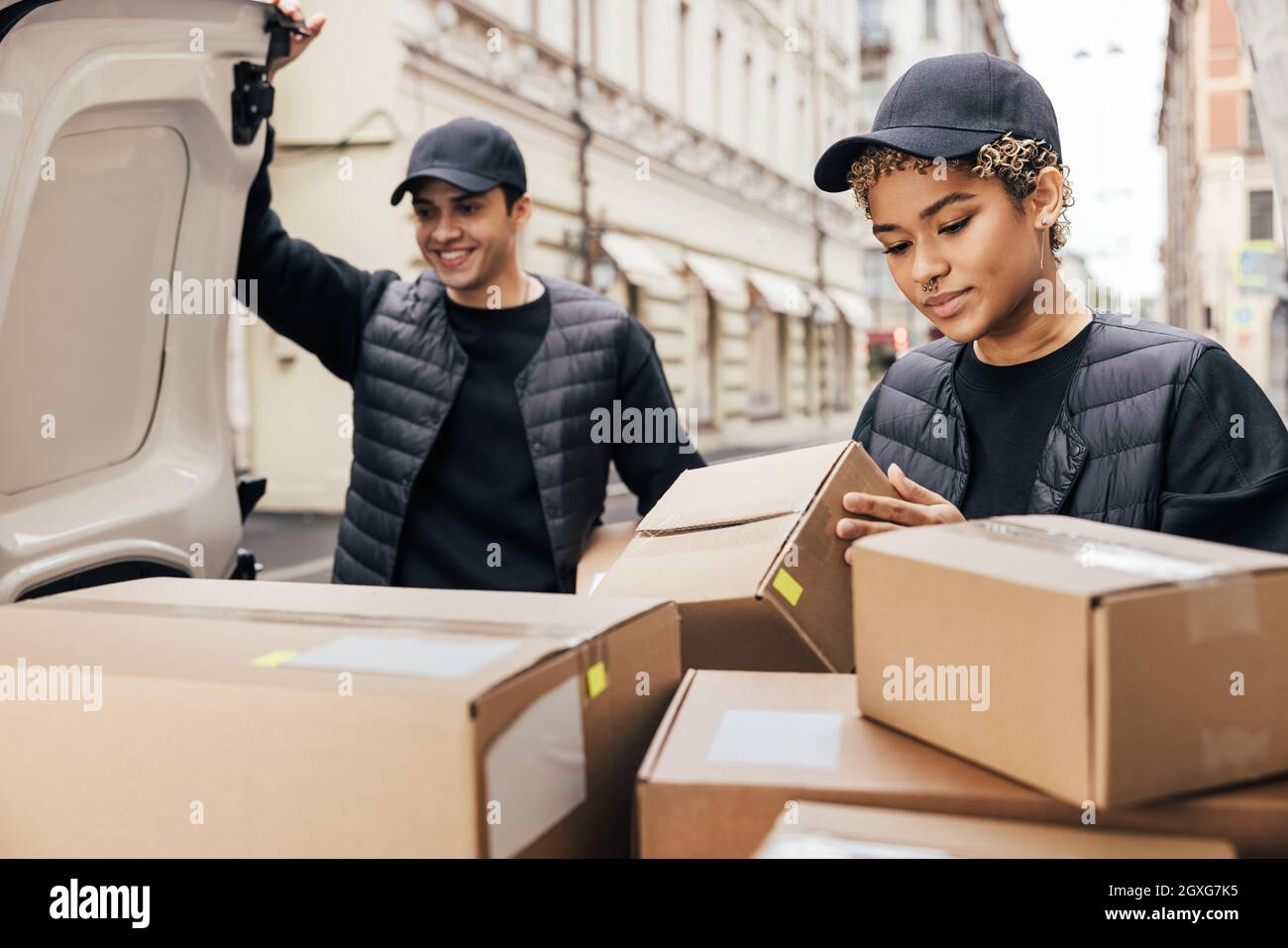 Two delivery people working at van trunk. Woman checking information on ...