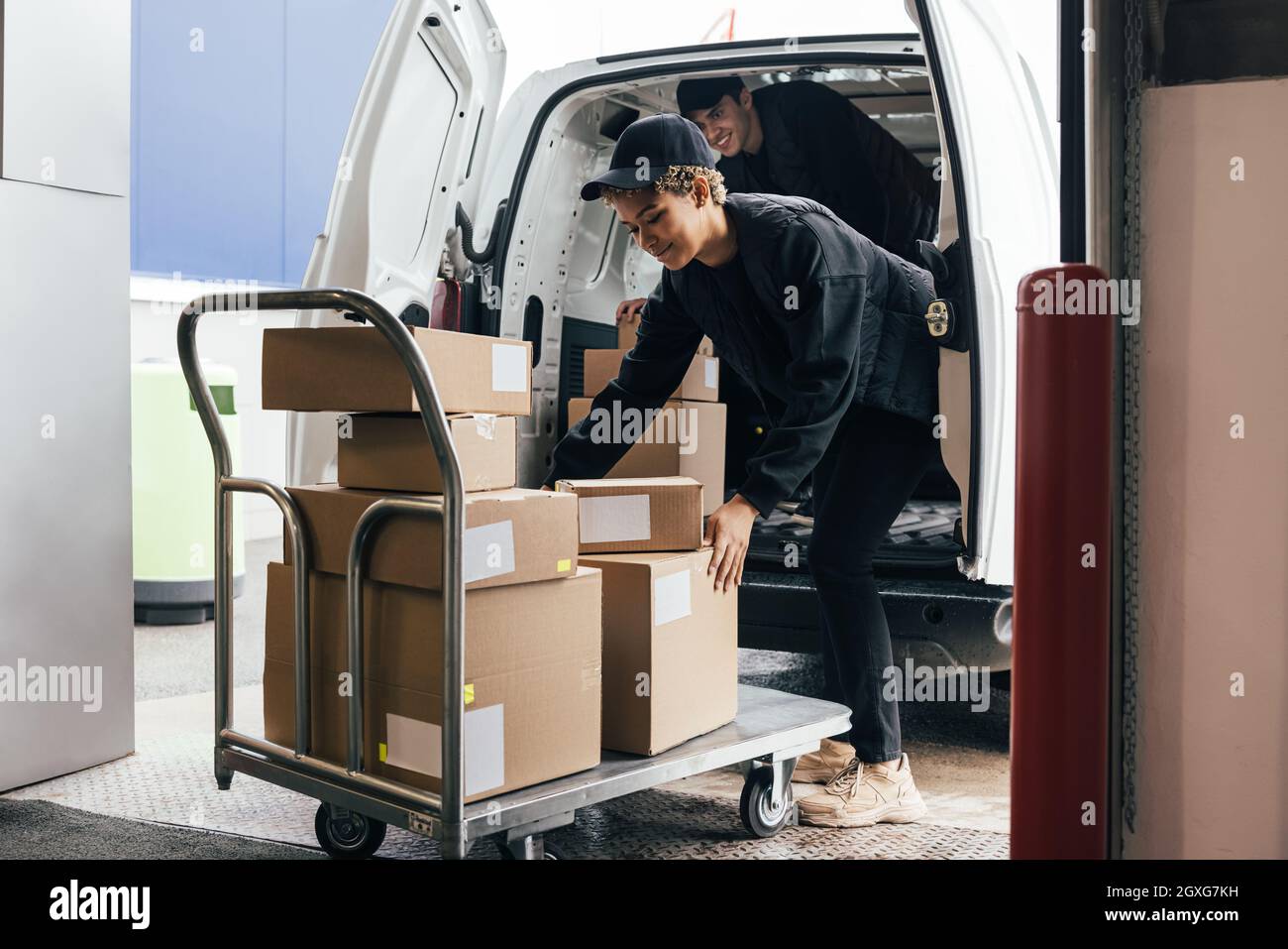 Female courier loads cardboard boxes from a cart into a van while a ...