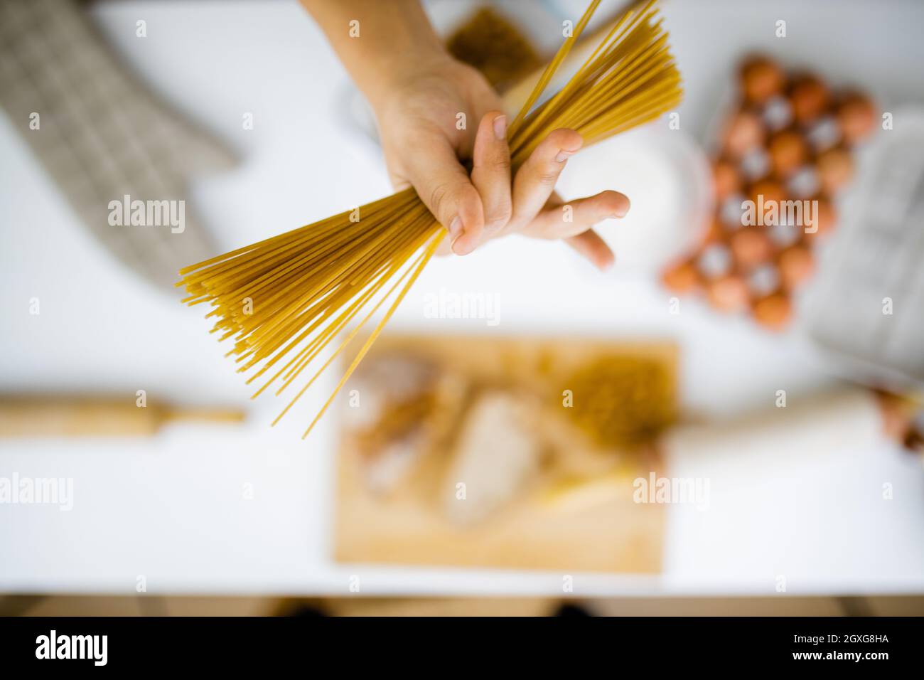 Female hand holding uncooked spaghetti above blurry ingredients on ...